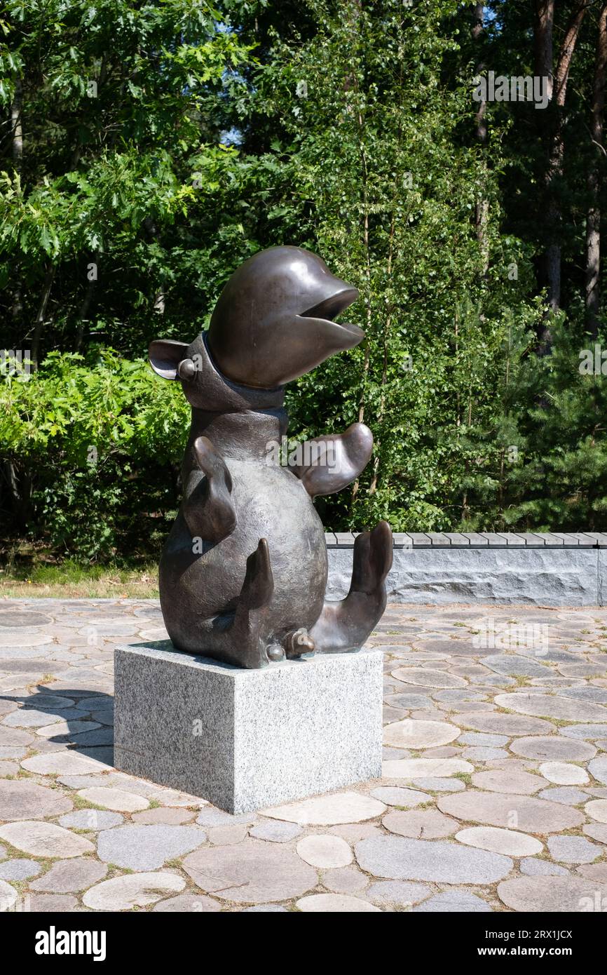 Sculpture of a creature on a plinth on a paved surface with trees ...