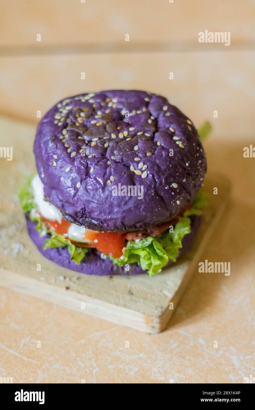close up photo of a home-made purple burger placed on a ceramic table ...