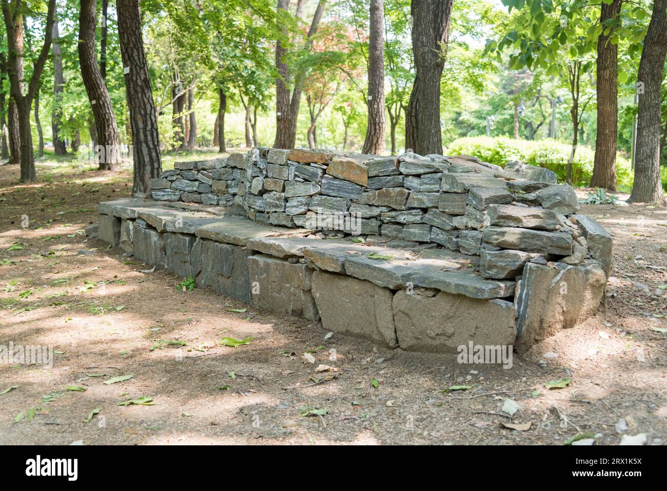 A bench made of stones or rocks piled together, in a garden of trees ...