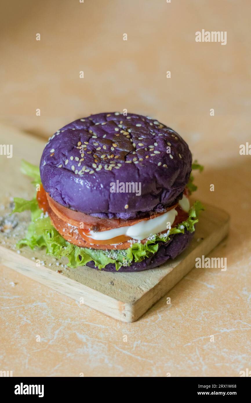 close up photo of a home-made purple burger placed on a ceramic table ...