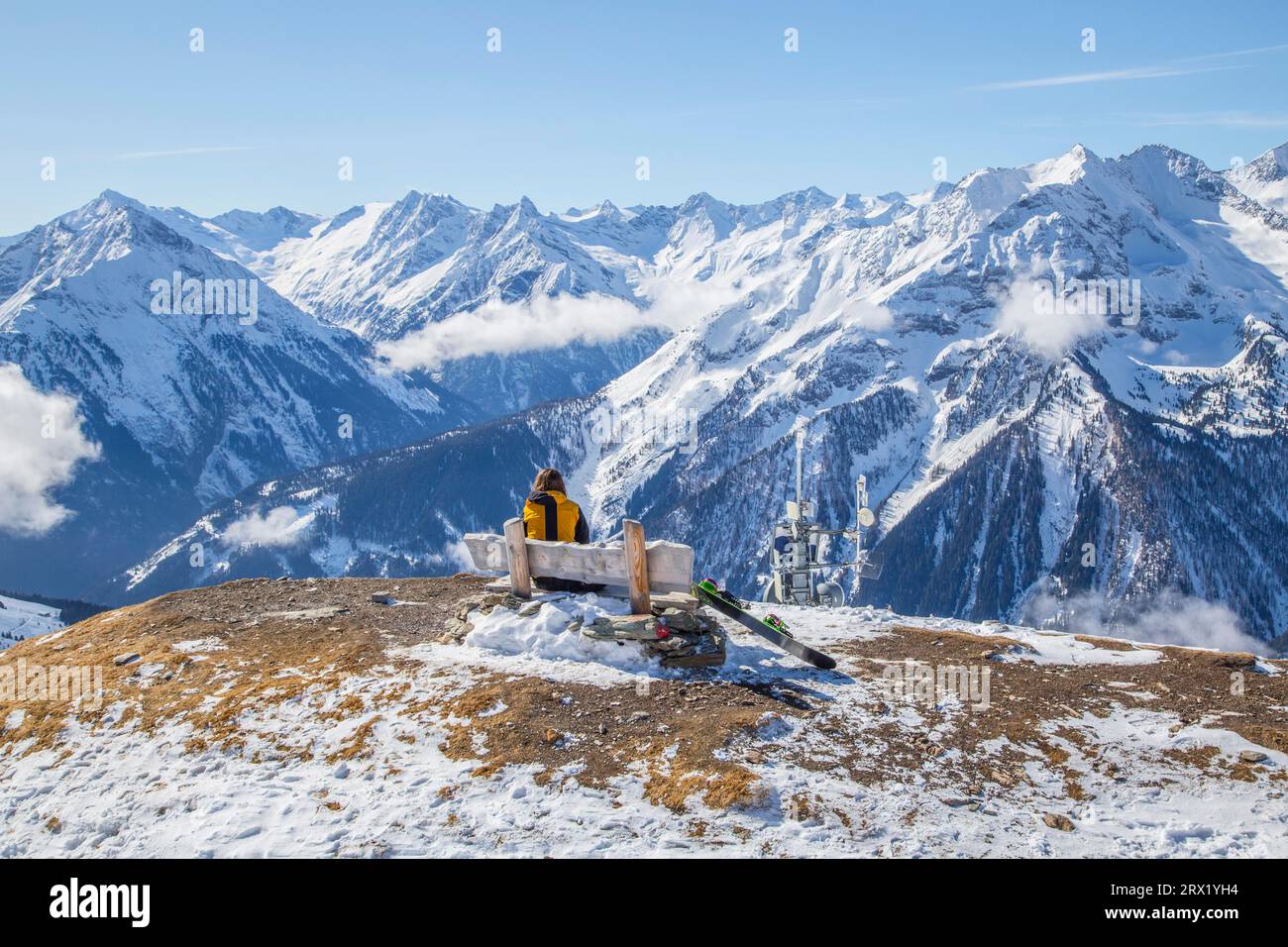 Skier sits on a bench and looks at the alpine chain, near the mountain ...