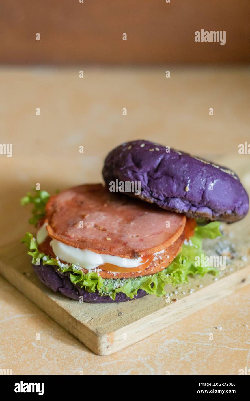 close up photo of a home-made purple burger placed on a ceramic table ...