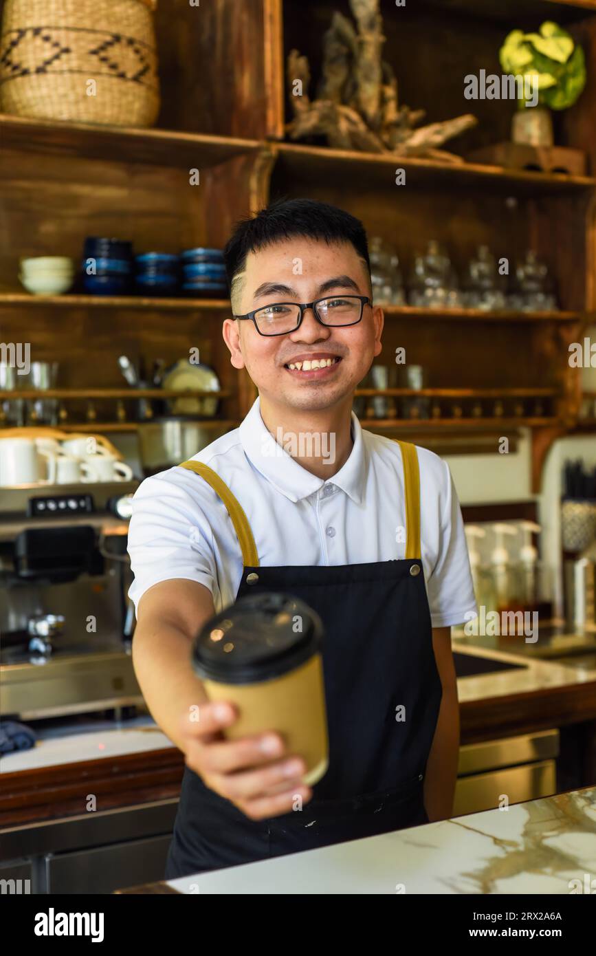 Vietnamese smiling waiter holding paper cups with coffee in a cafe ...
