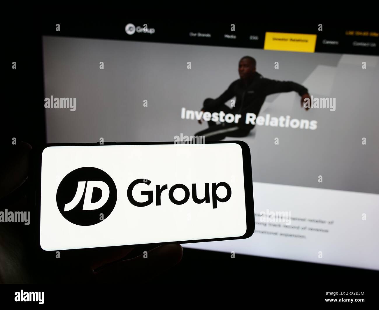 Person holding mobile phone with logo of British retail company JD Sports Fashion plc on screen ...