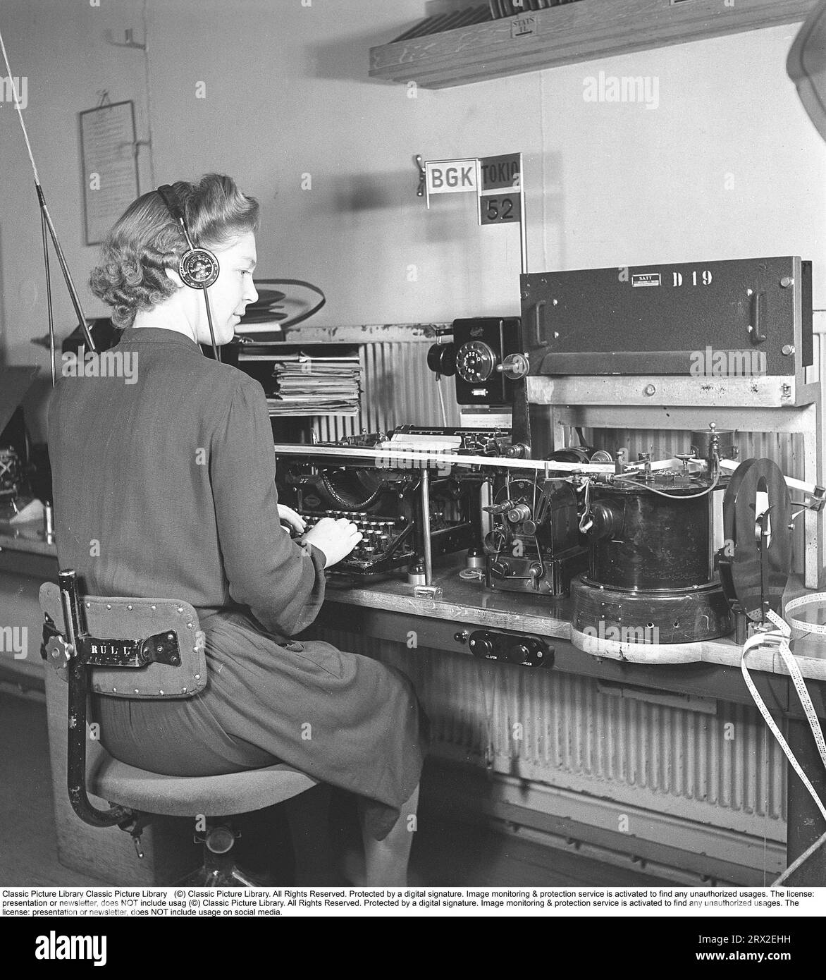 In the 1940s. A woman wearing headphones at a quirky workstation where she sits at a typewriter ...