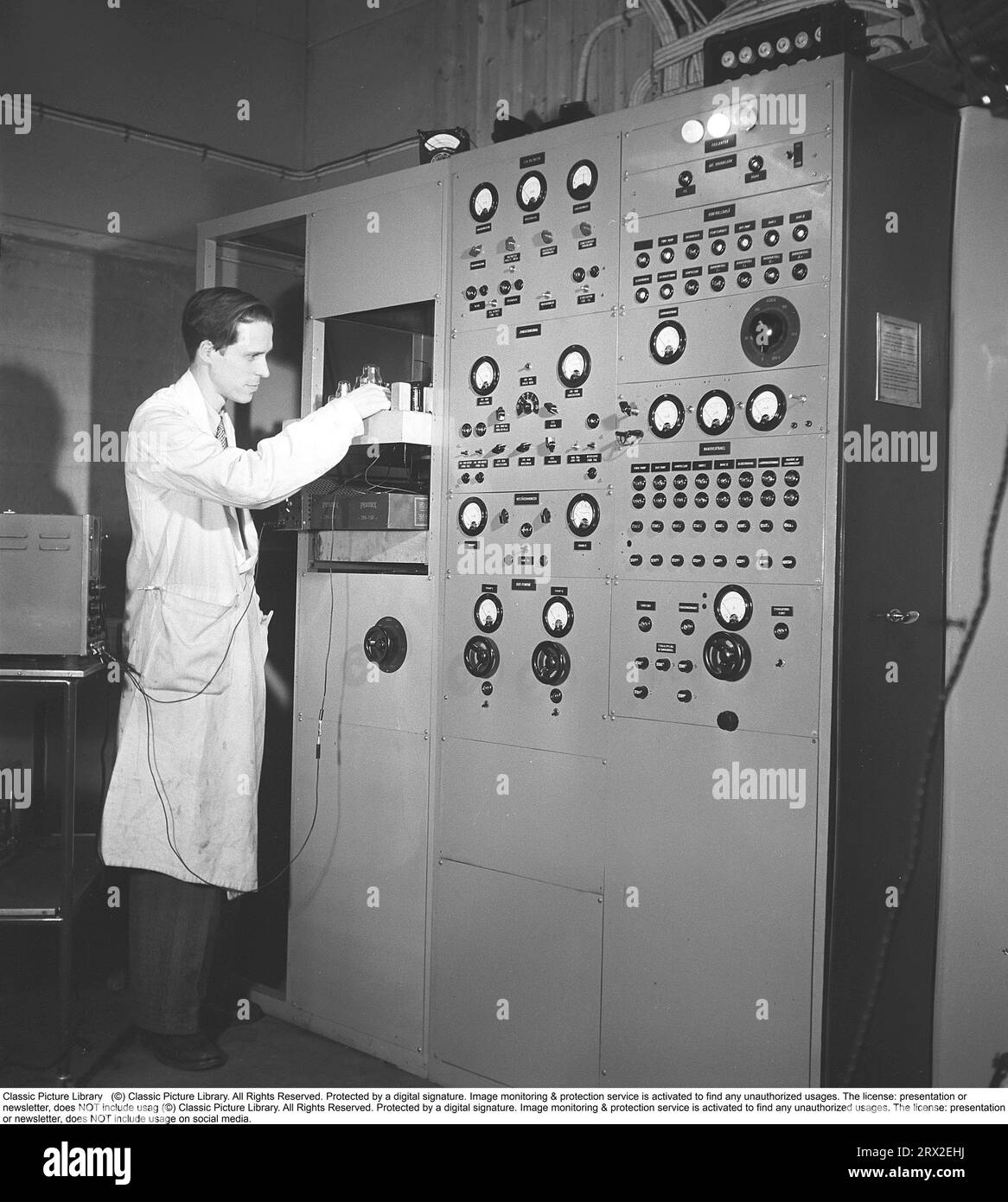Man and machine in the 1940s. An engineer dressed in a white coat at an ...