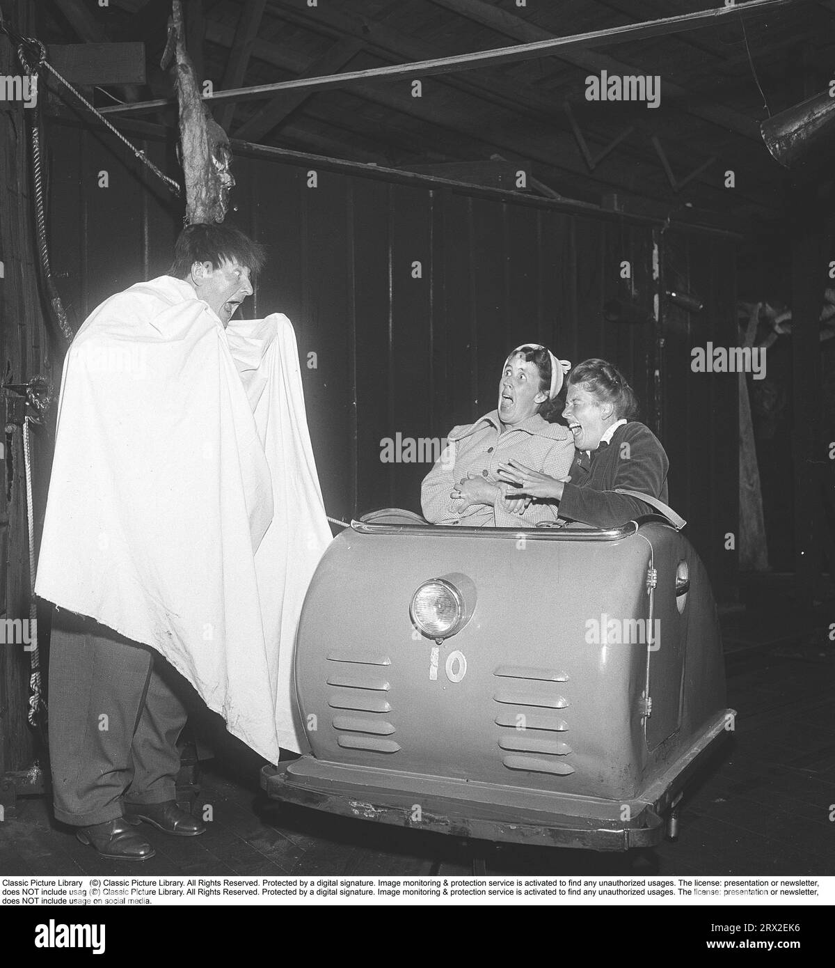 Amusement park in the 1950s. Two women are riding the scary ride and ...