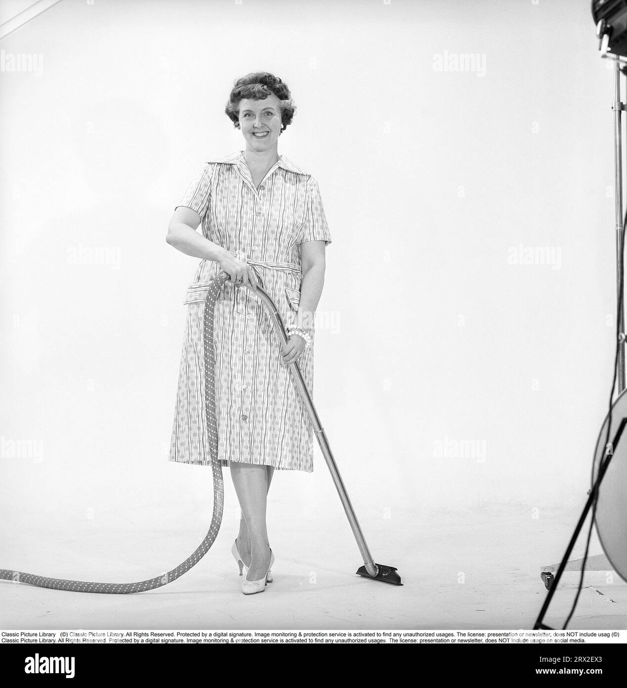 Cleaning day in the 1960s. A woman is standing holding a vacuum cleaner ...
