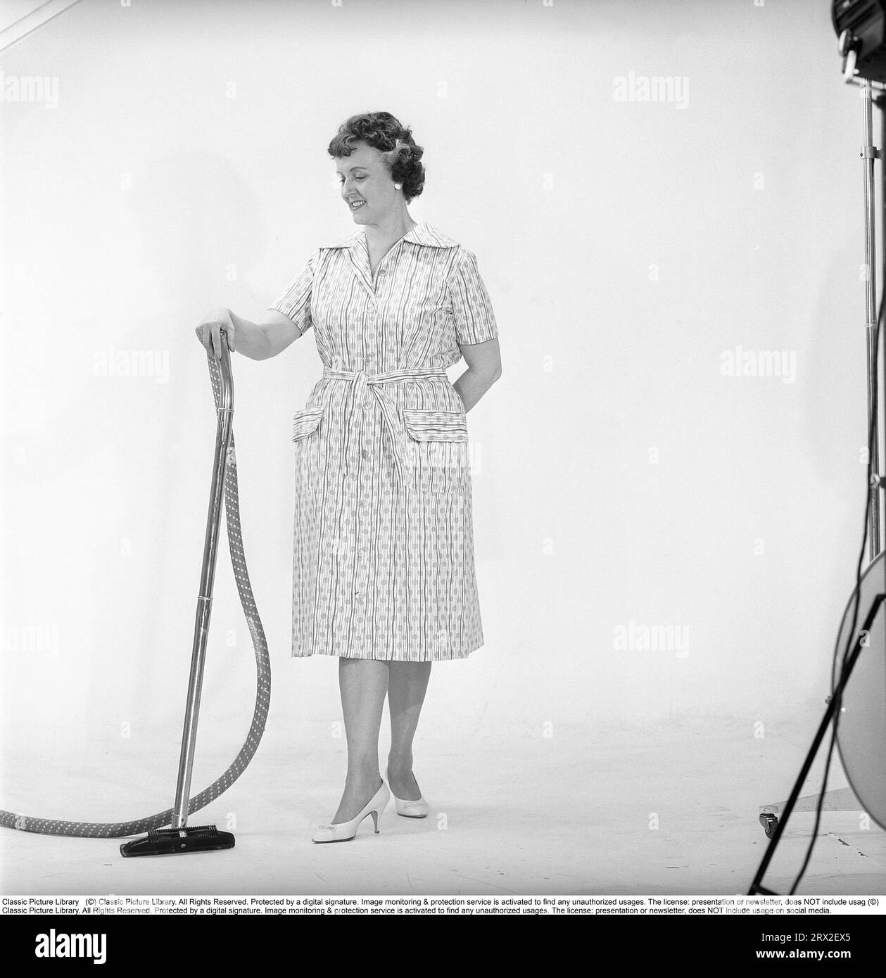 Cleaning day in the 1960s. A woman is standing holding a vacuum cleaner ...