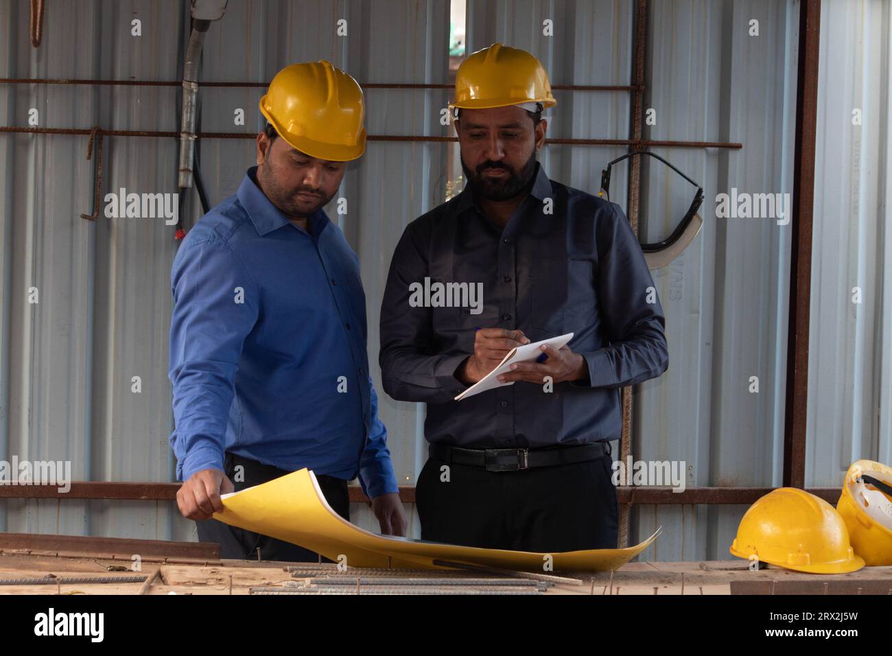 Civil engineer holding a blueprint while colleague is taking notes into ...