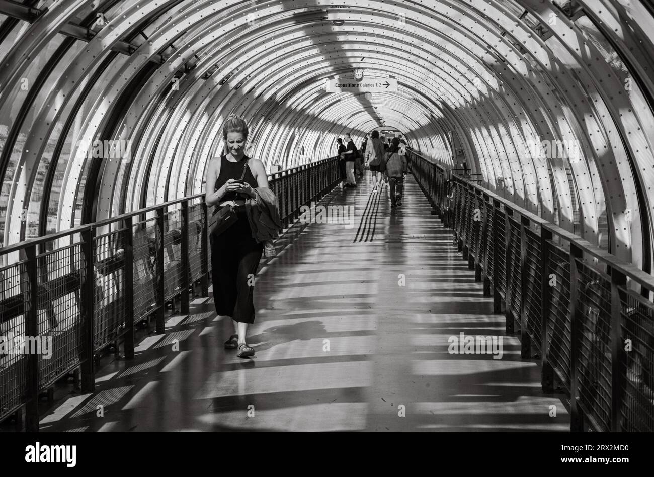 A woman walks along a high level glass-enclosed walkway on a sunny day ...