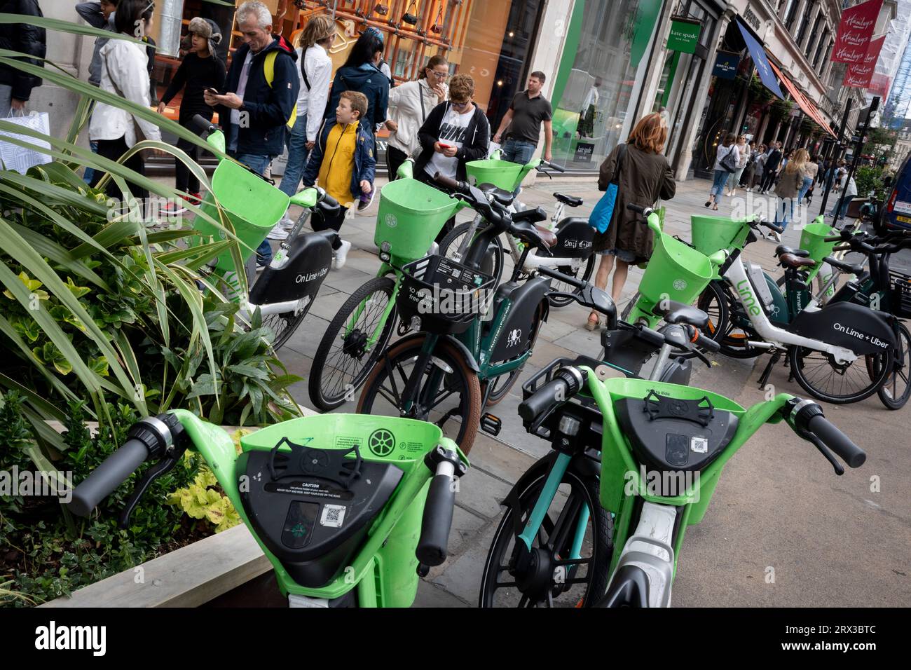 Members of the public walk past many Lime rental bikes that are stood ...