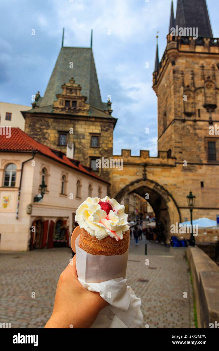 Female hand holding traditional czech cake trdelnik with whipped cream ...