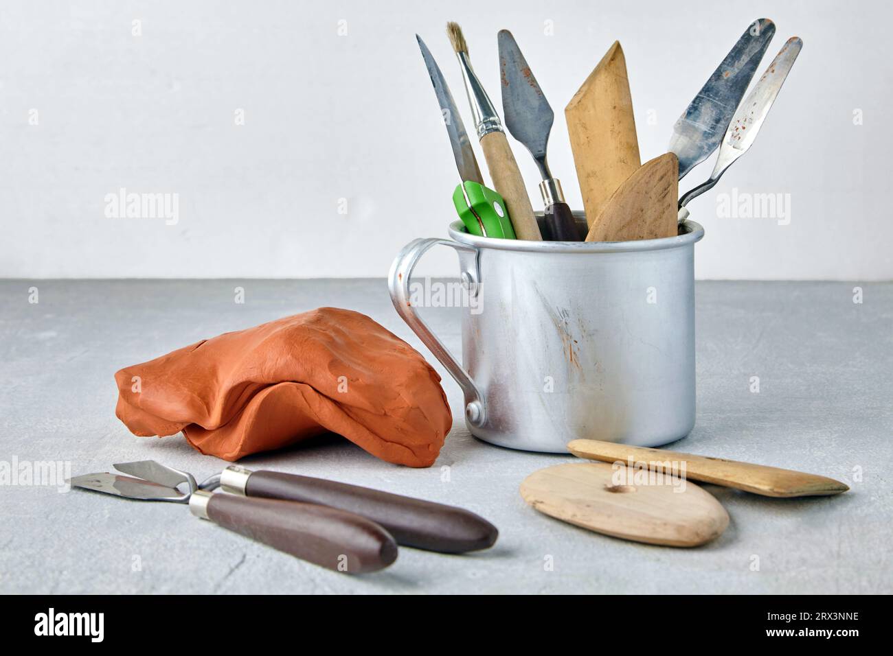 A set of modeling tools in a metal mug and a piece of brown plasticine ...