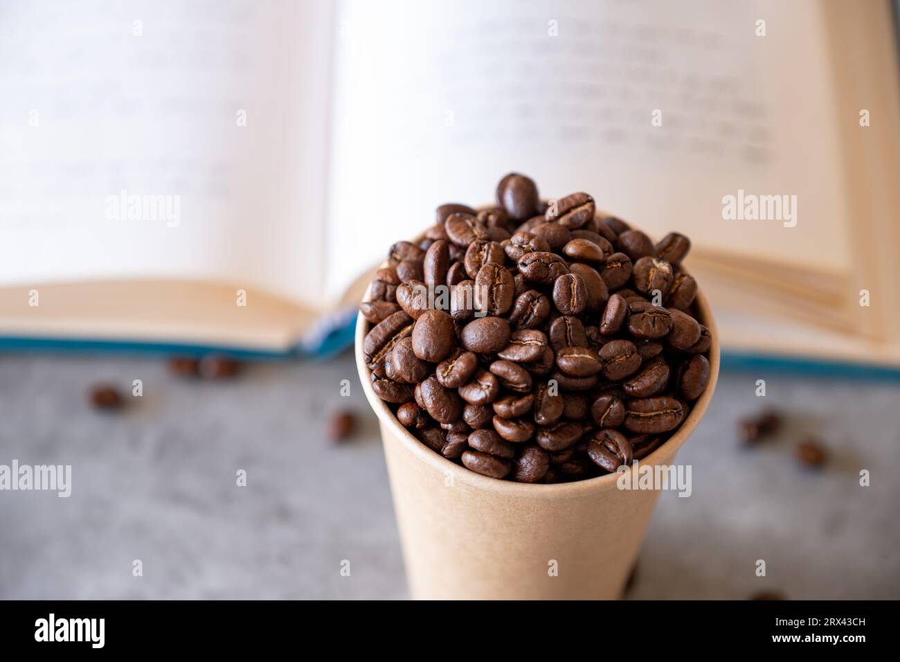 paper cup of coffee full of coffee beans with grey background and book ...