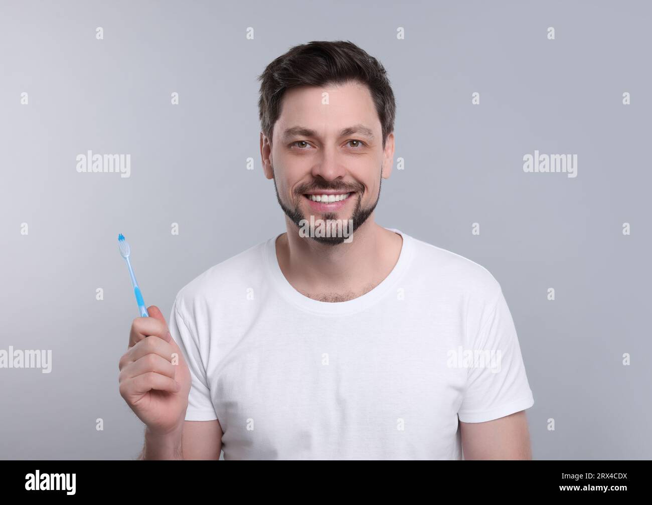 Happy man holding toothbrush on light grey background Stock Photo - Alamy