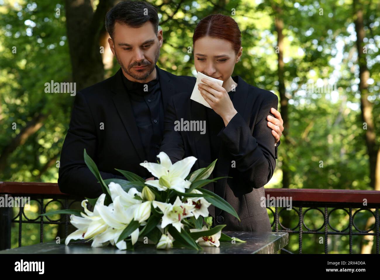Sad couple mourning near granite tombstone with white lilies at ...