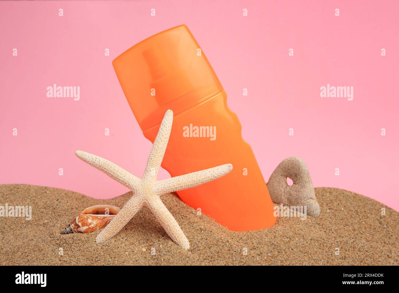 Sand with sunscreen, starfish, stone and seashell against pink ...