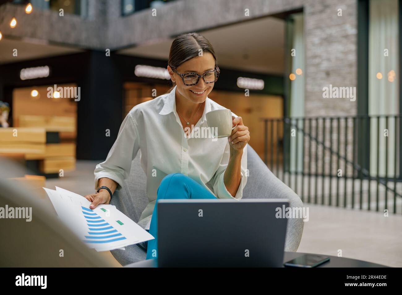 Smiling female analyst drinks coffee working with documents and use ...