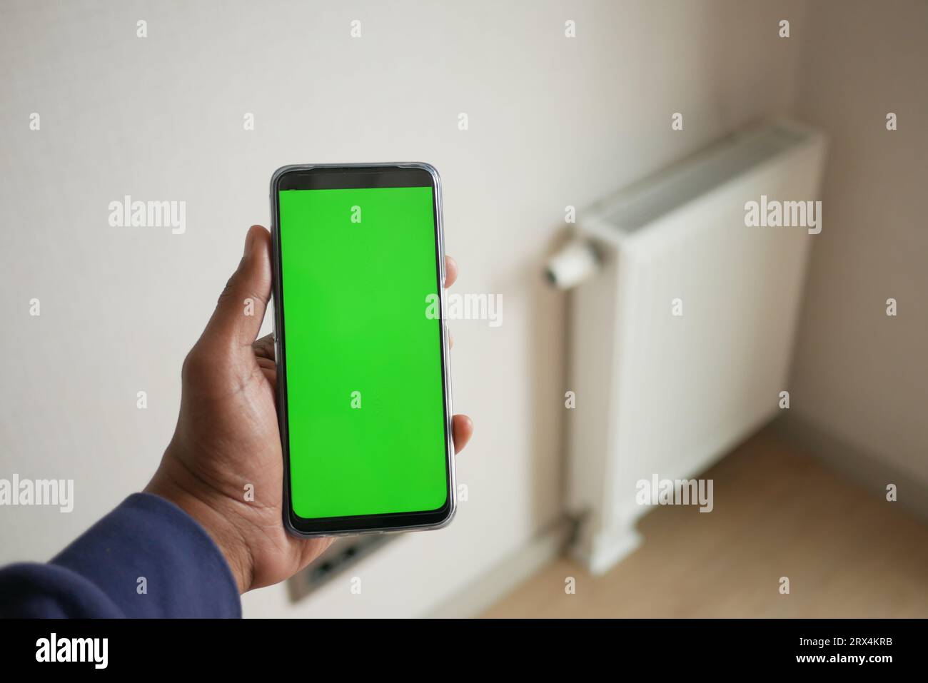 holding smart phone with green screen against White radiator on grey ...