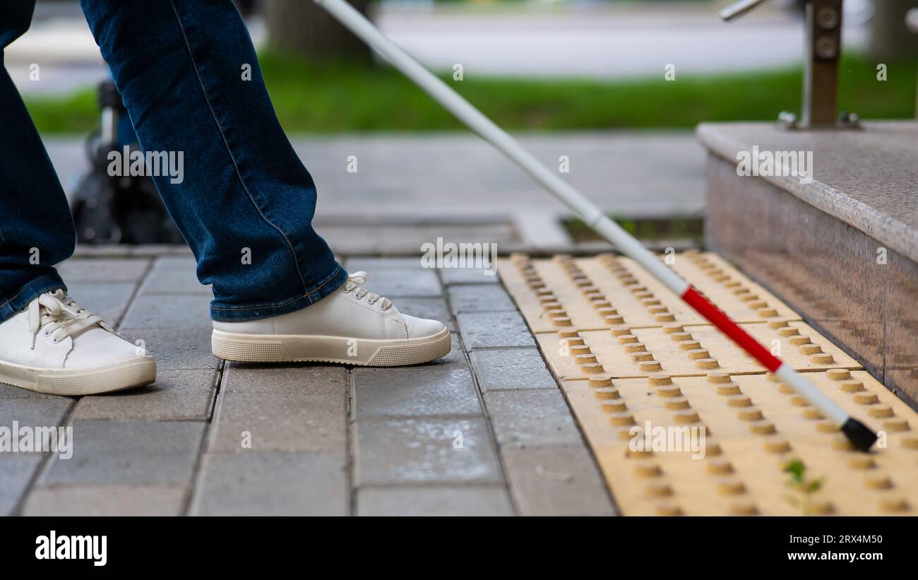 Close-up of female foot, walking stick and tactile tiles. Blind woman ...