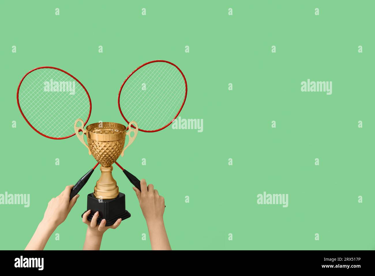 Female hands with gold cup and badminton rackets on green background ...