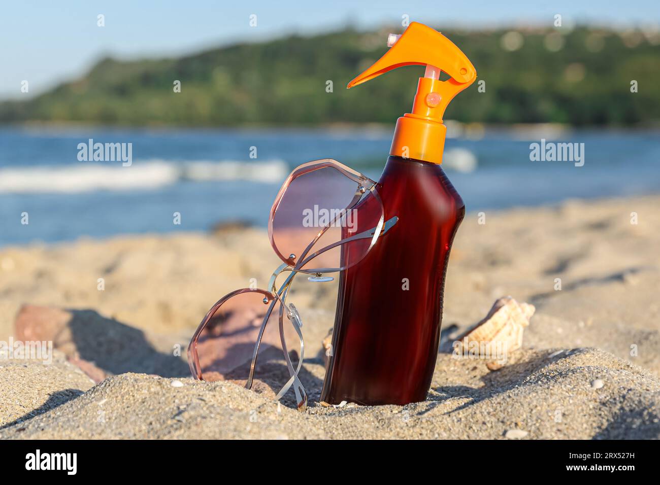 Bottle of sunscreen cream with sunglasses on sand near ocean at beach ...