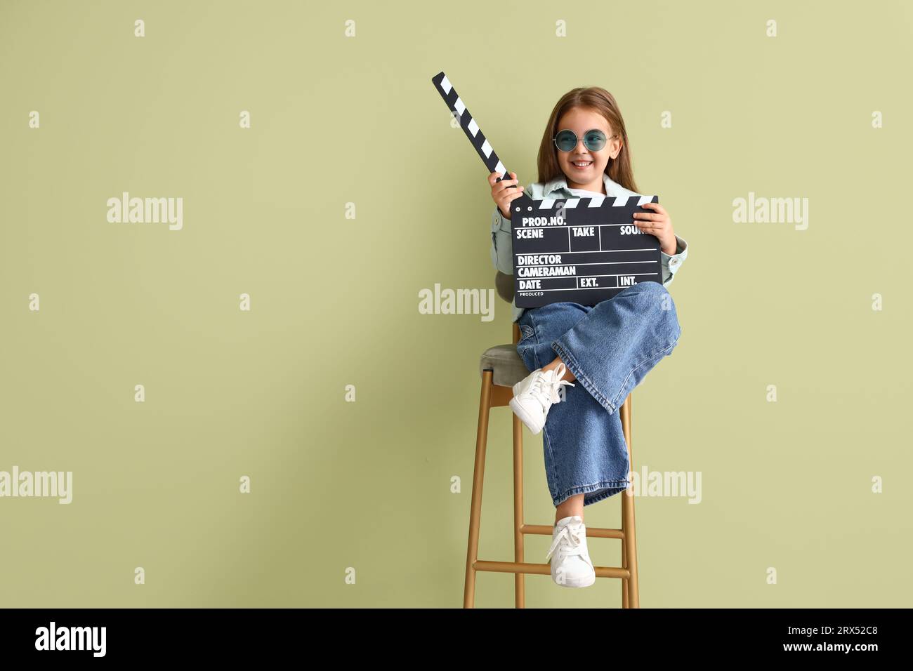 Cute little girl in sunglasses with movie clapper sitting on green ...