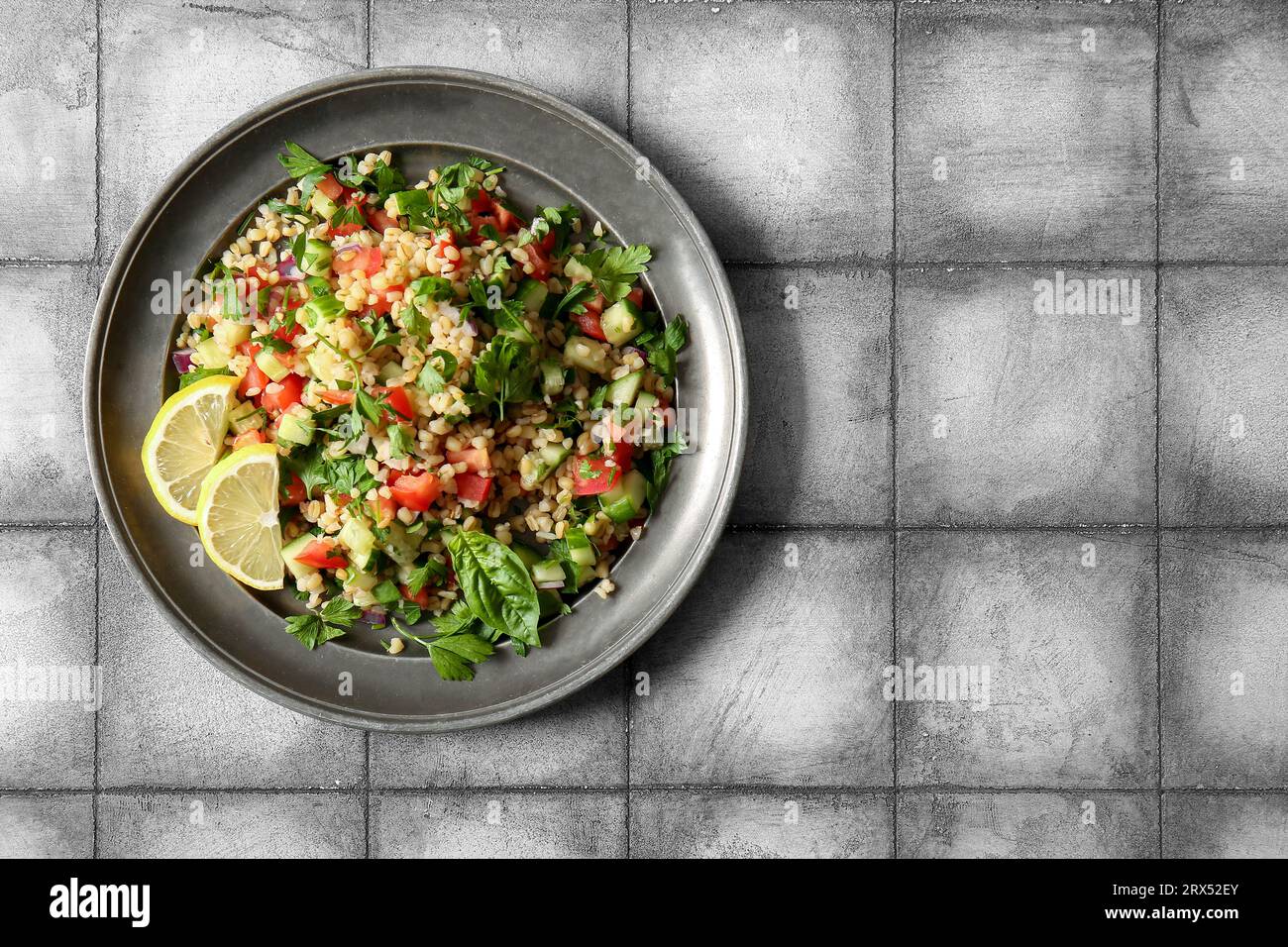Plate with delicious tabbouleh salad and lemon slices on tile grey ...