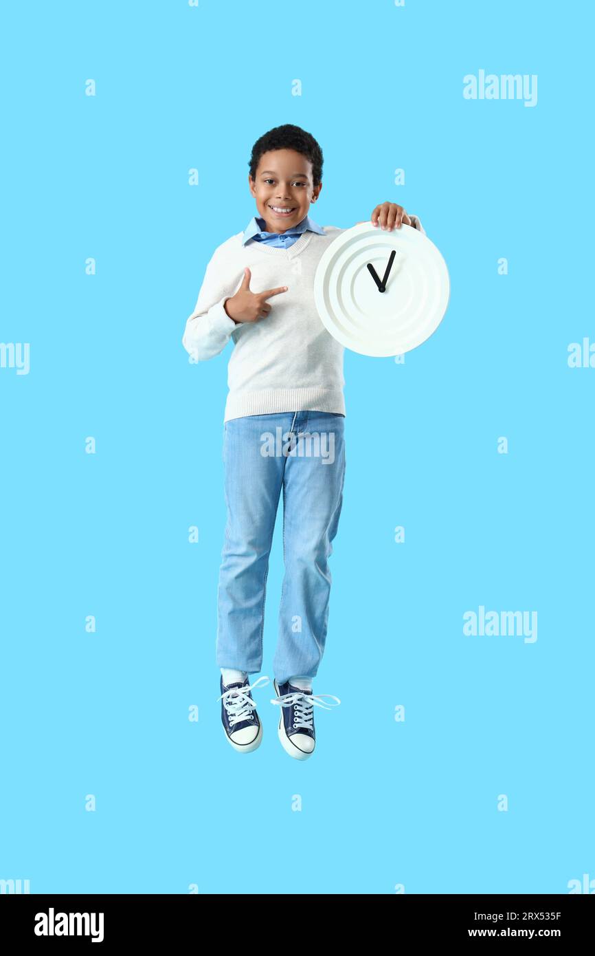 African-American little boy with clock jumping on blue background Stock ...