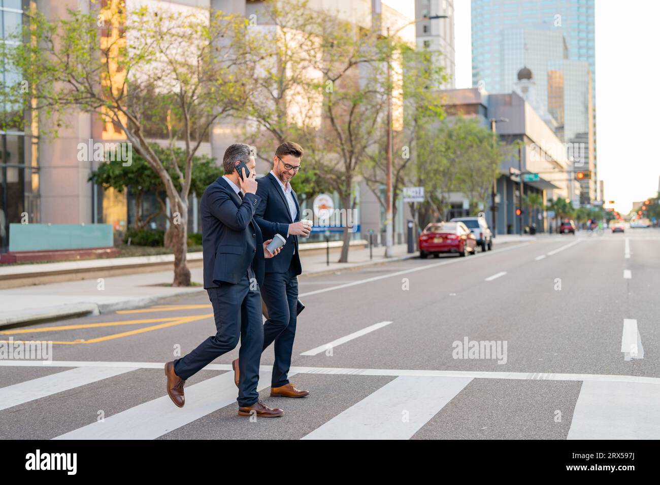 Photo of businessmen in suits walking outdoor through city street. Two ...