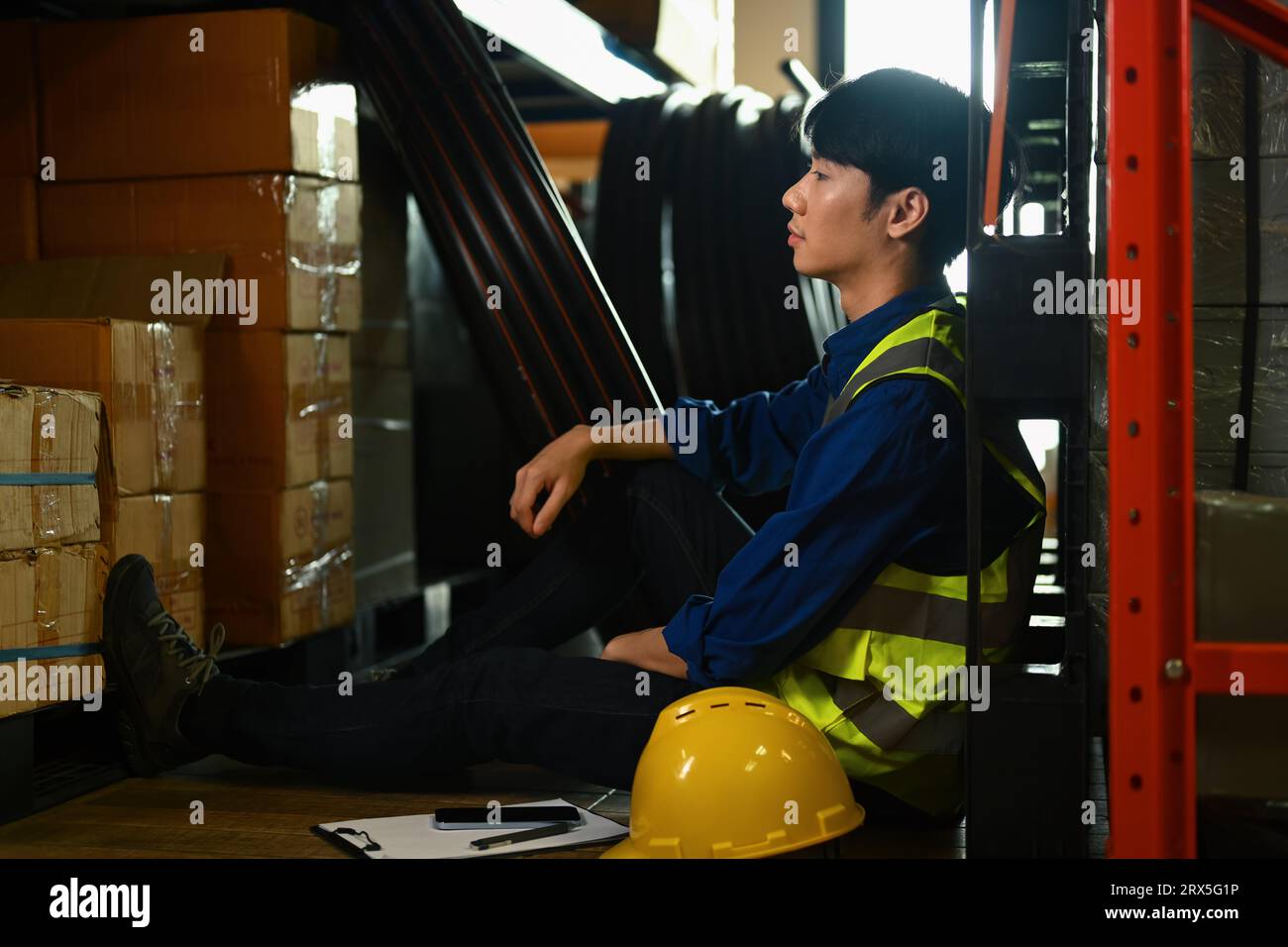 Overworked male worker leaning against shelf in a warehouse, taking a ...