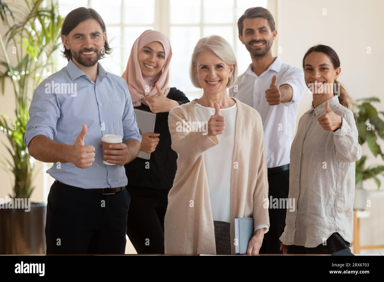Five multicultural staff smiling showing thumbs up posing for camera ...