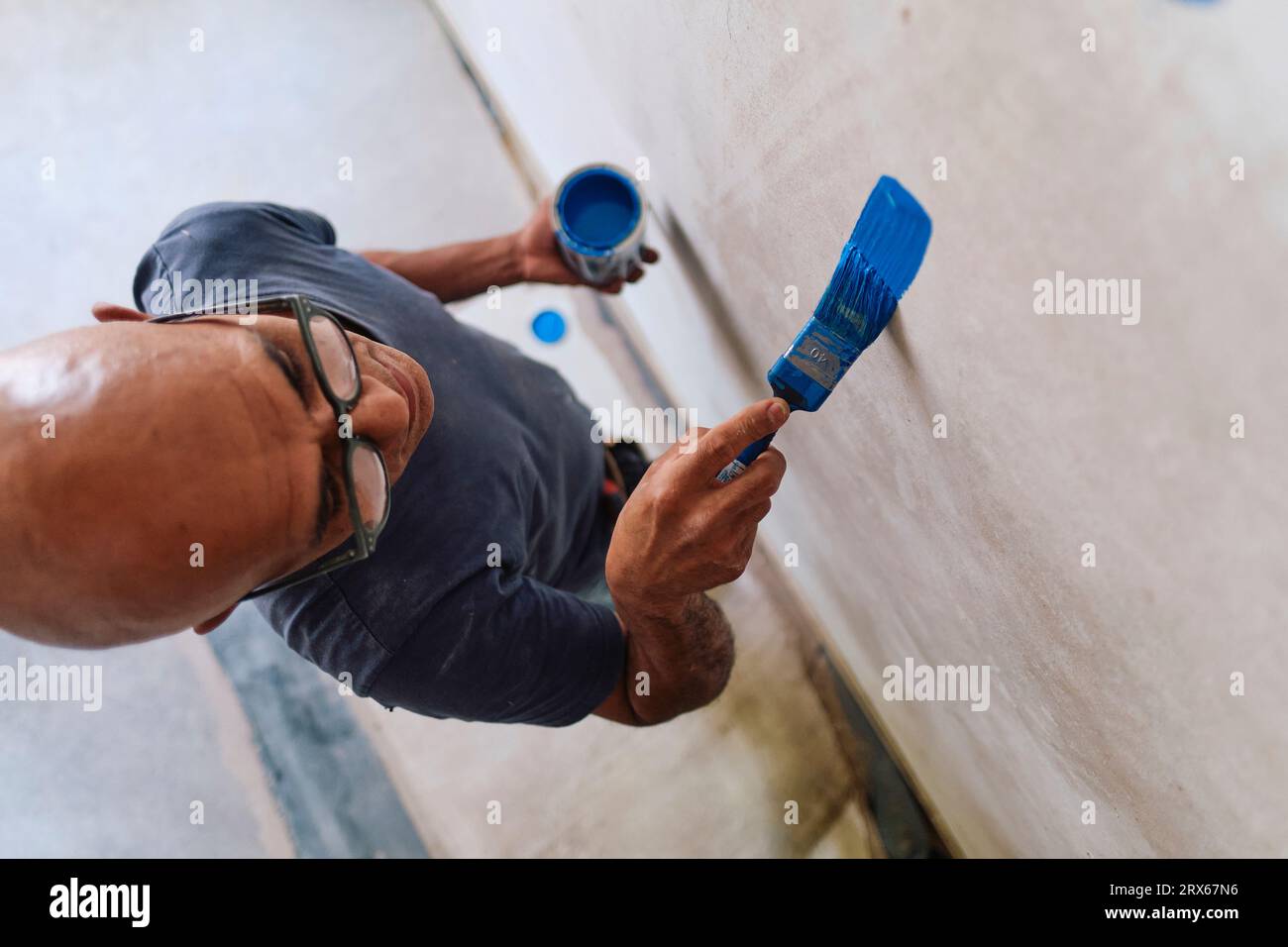 Bald construction worker applying blue paint on wall Stock Photo - Alamy