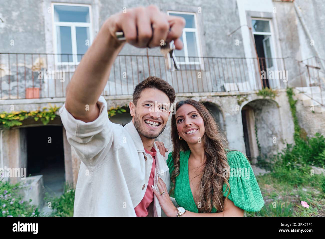 Happy couple with keys standing together in front of house Stock Photo ...