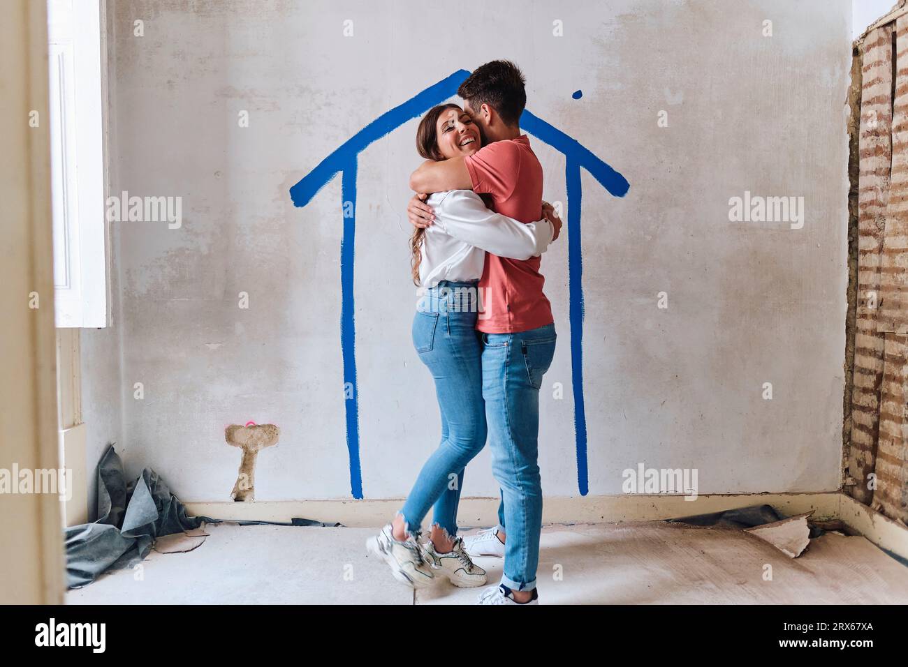 Happy couple hugging each other in front of wall at construction site ...