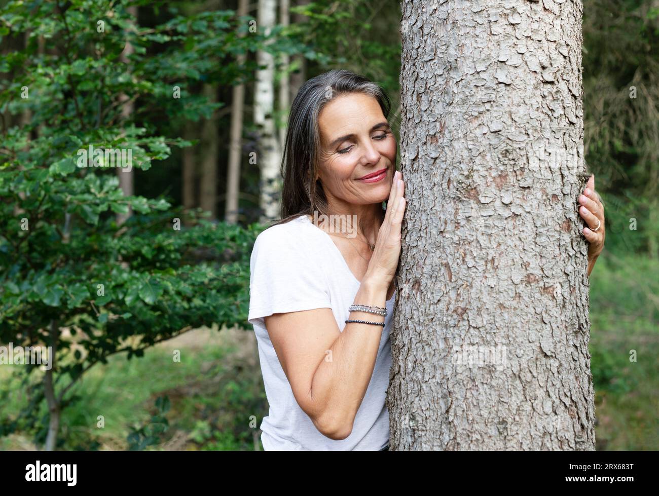 Smiling woman hugging tree in forest Stock Photo - Alamy