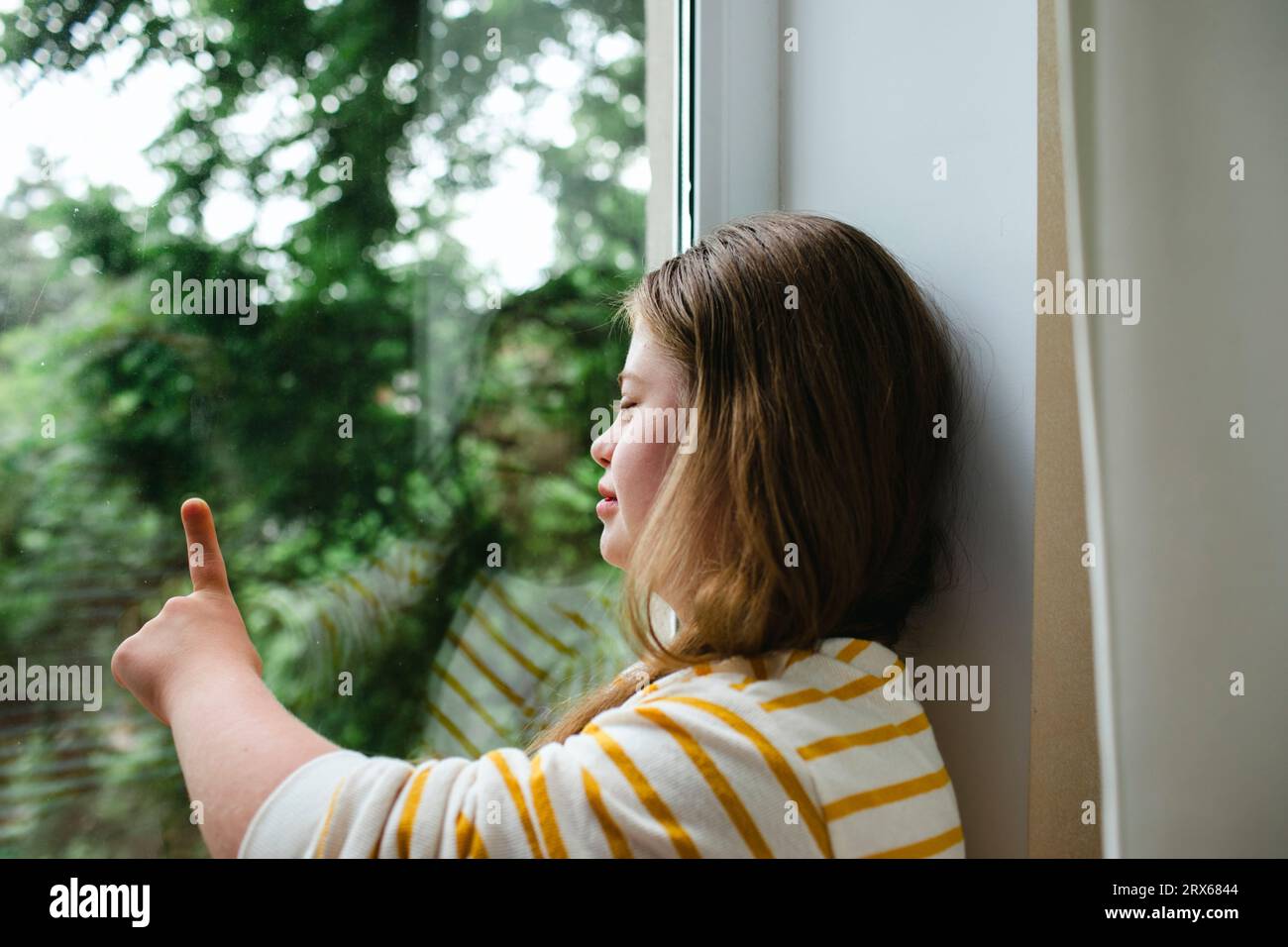 Teenage girl with down syndrome touching window glass Stock Photo - Alamy