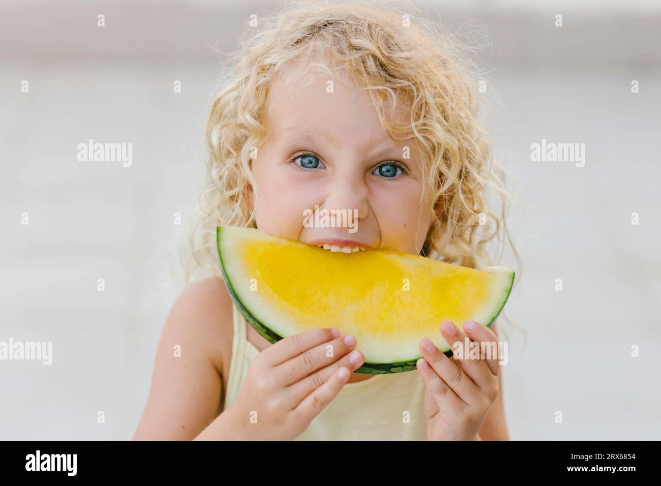 Blond girl biting slice of yellow watermelon Stock Photo - Alamy