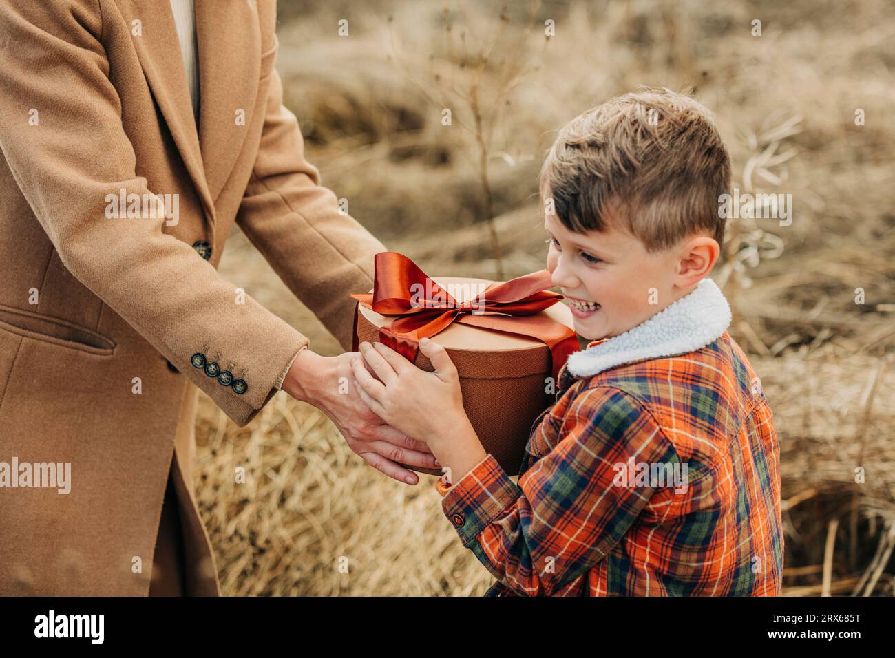 Mother giving gift box to happy son in field Stock Photo - Alamy