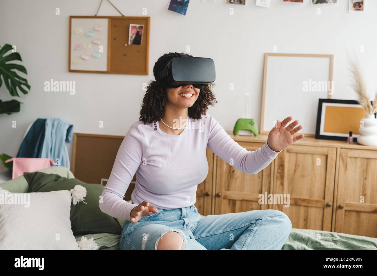 Happy girl wearing virtual reality simulators gesturing on bed at home ...
