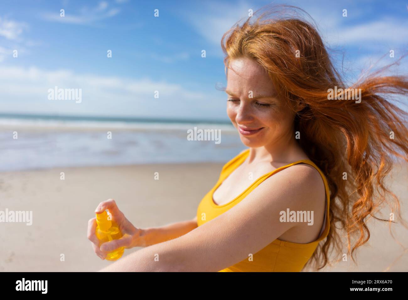 Smiling woman spraying suntan lotion on hand at beach Stock Photo - Alamy