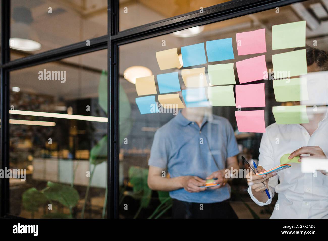 Businessmen sticking colorful adhesive notes on glass wall at office ...