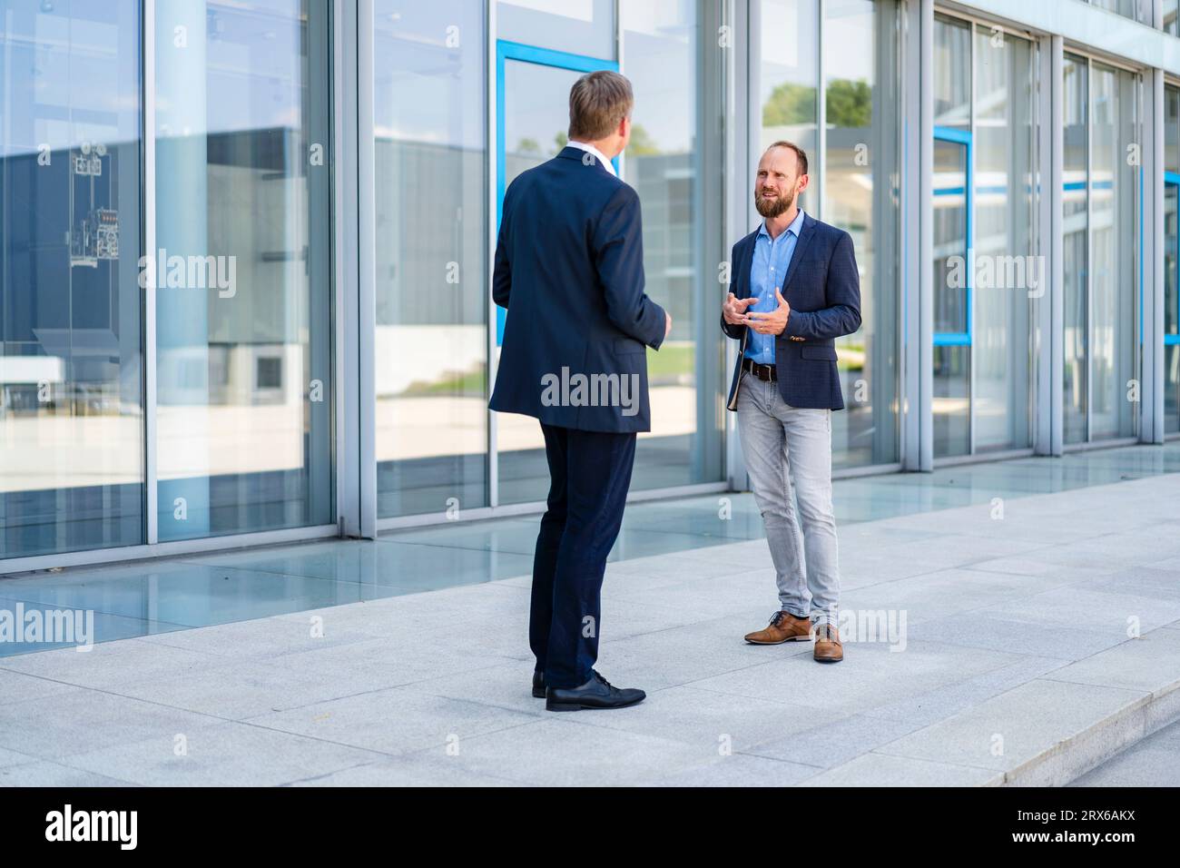 Two businessmen standing in front of office building talking Stock ...