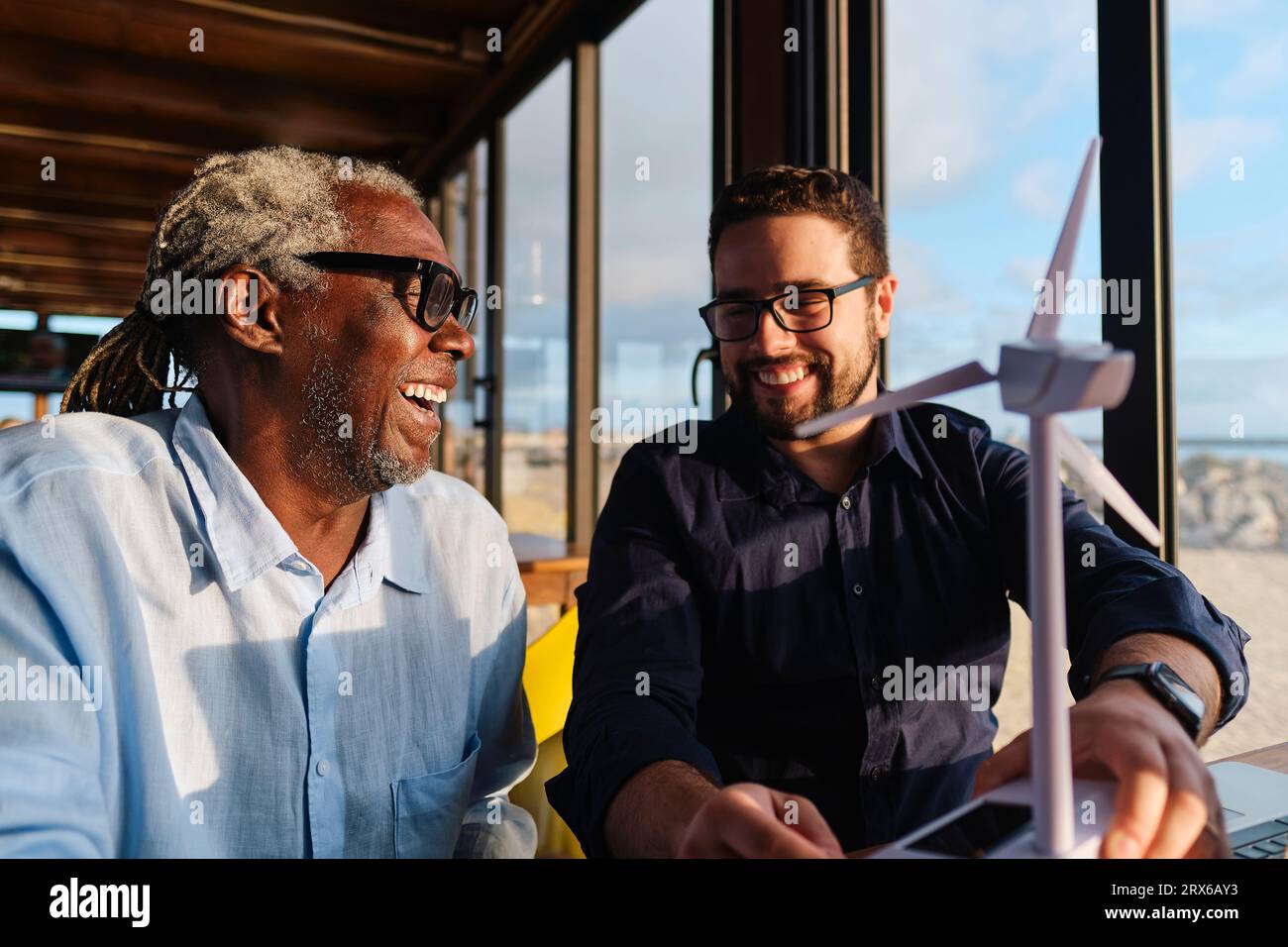 Happy engineers having discussion over wind turbine model in restaurant ...