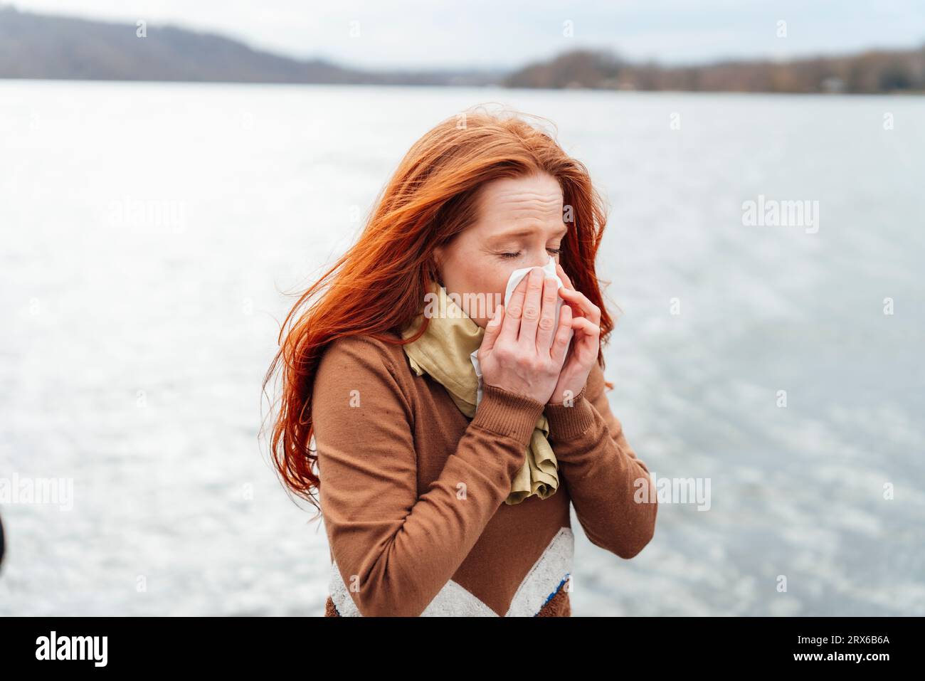 Redhead woman blowing nose in front of lake Stock Photo - Alamy