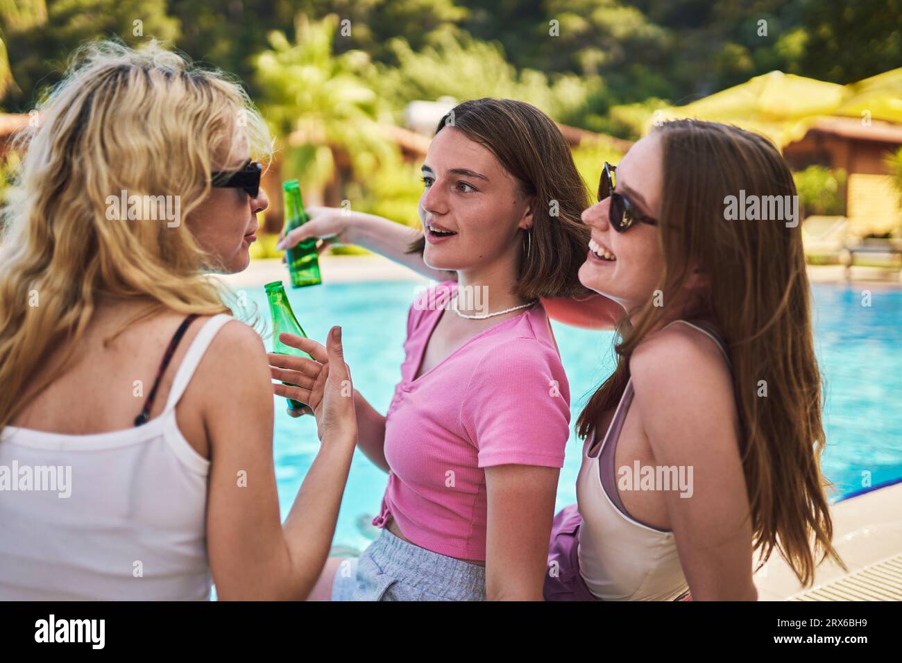 Smiling friends with bottles sitting by swimming pool Stock Photo - Alamy