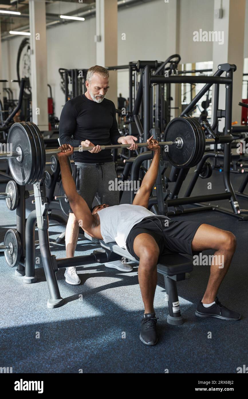 Mature trainer helping man for strength training in gym Stock Photo - Alamy
