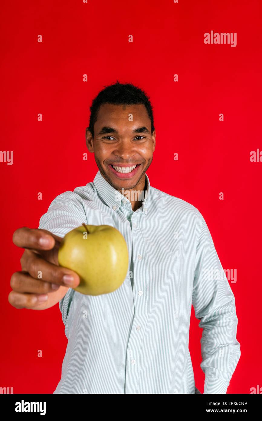 Smiling man showing green apple against red background Stock Photo - Alamy