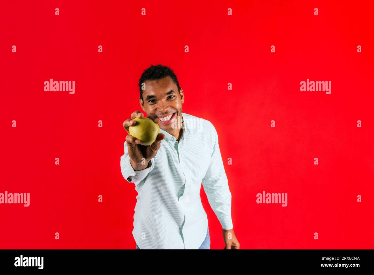 Happy man showing apple standing against red background Stock Photo - Alamy